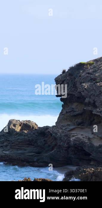 Ocean waves crash against rugged rocks under clear skies, showcasing ...