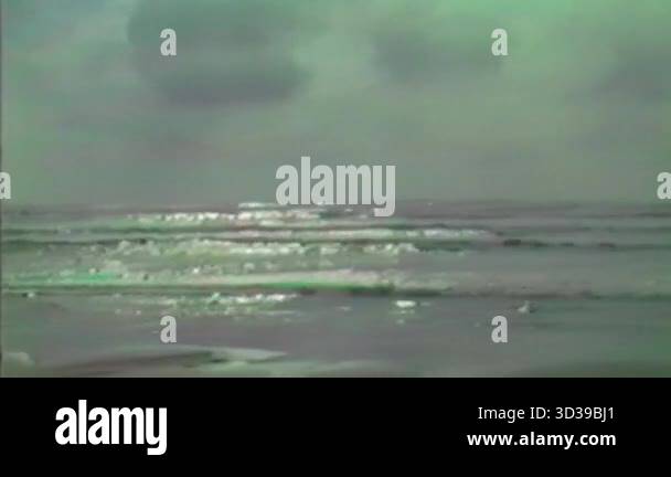 A wide, reflective shoreline at low tide stretches beneath a hazy sky ...