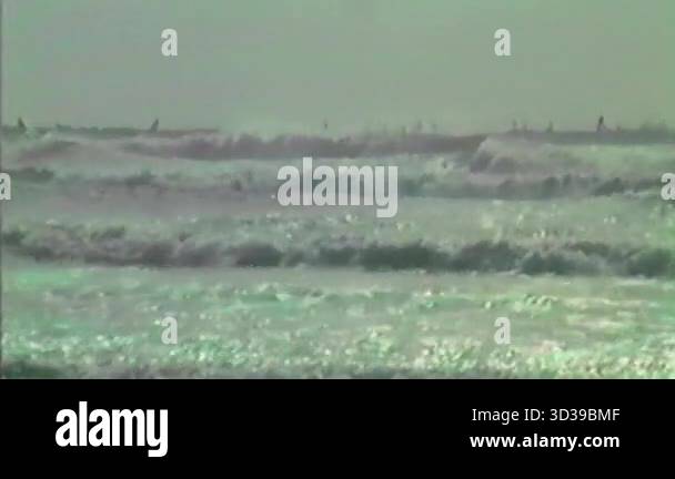 Powerful waves crash against the shore as a few distant swimmers brave ...