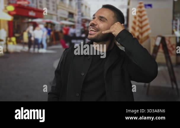 Man makes phone gesture with hand and smiling face on busy street with ...