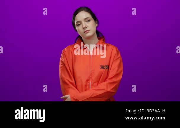Woman in orange prison jumpsuit stands against a vivid purple ...
