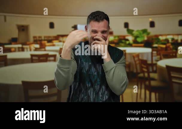 Young man laughing joyfully in a restaurant with round tables and ...