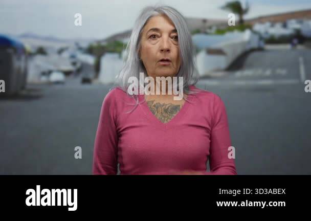 Woman with gray hair covers mouth in surprise on an outdoor street ...