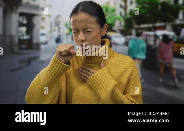 Woman coughing on city street wearing yellow sweater outdoors in urban ...