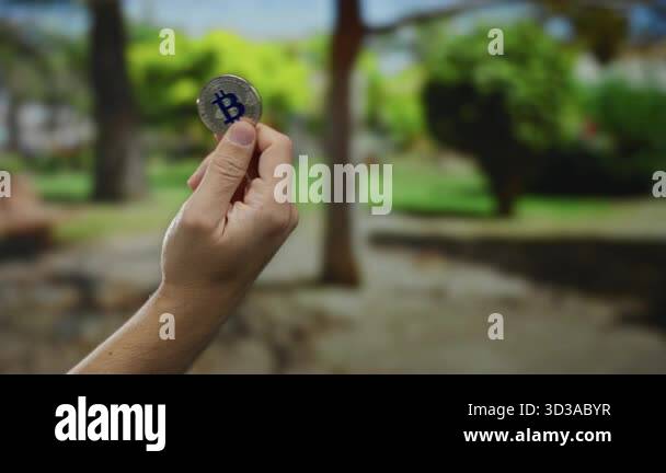 Man holding bitcoin outdoors with green park scenery in background ...