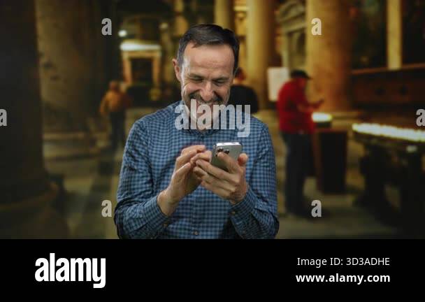 Man smiling while using smartphone inside church with blurred ...