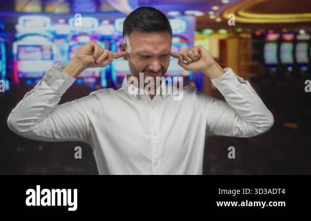 Hispanic man covering ears in a busy casino environment, expressing ...