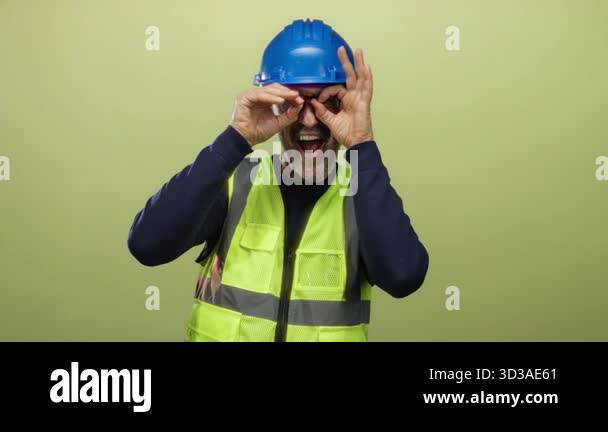 Man wearing blue helmet and yellow vest gestures playfully against ...