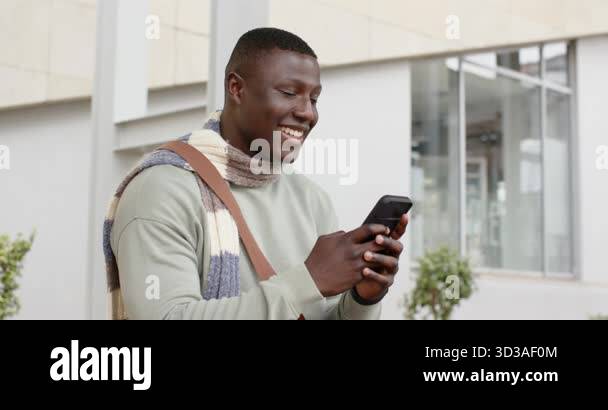African American man by glass wall scrolling phone reading funny text ...