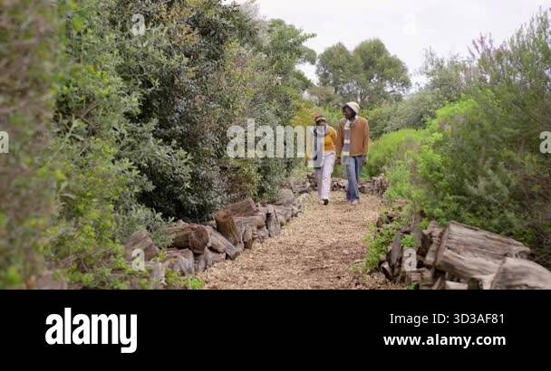 African American couple walking along wood-chip path, woman pointing at ...