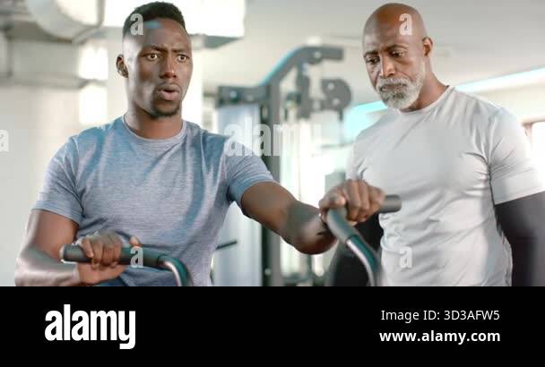 African American male trainer guiding client starting pedaling air bike ...
