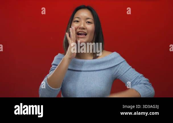 Woman shouting against a vibrant red wall background, expressing ...