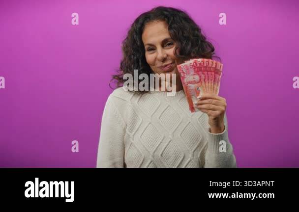 Woman holding chinese yuan banknotes smiling against a purple wall ...