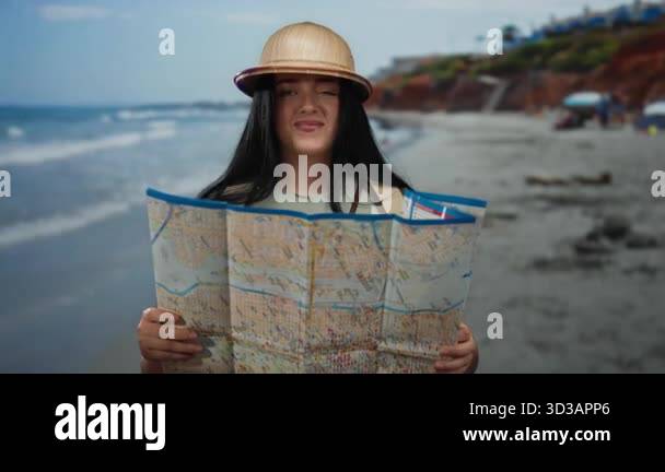 Woman exploring the seaside with a map, wearing a backpack and a hat ...