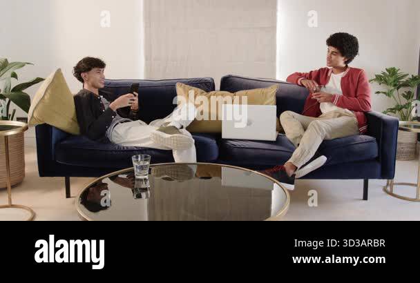 Diverse male friends leaning back at home showing phone sipping drink ...