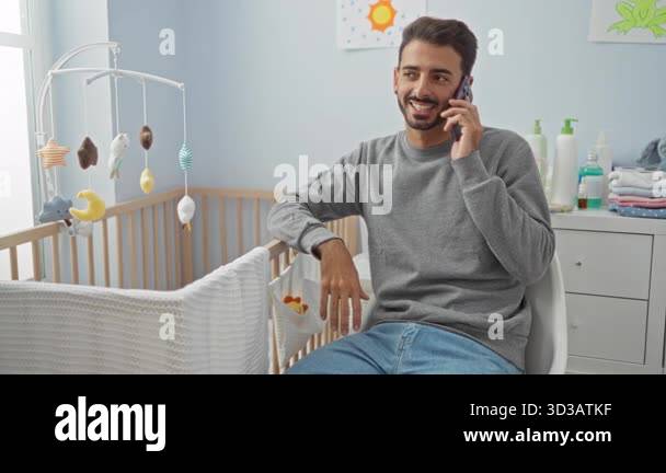 Young man talking on phone while sitting by cradle in cozy baby room ...