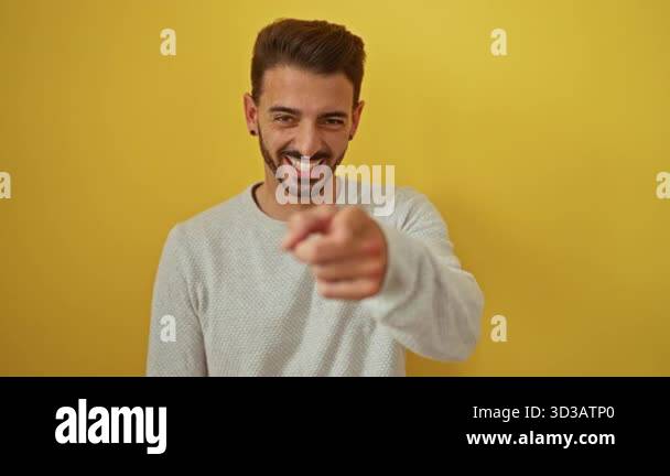 Young man laughing while pointing at camera against a vibrant yellow ...