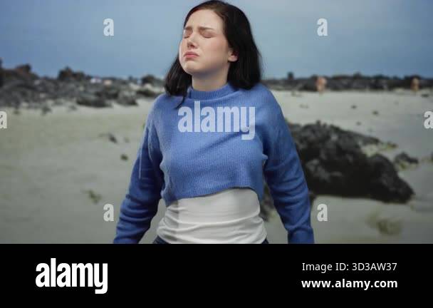 Woman standing on a rocky beach looking stressed with closed eyes in ...