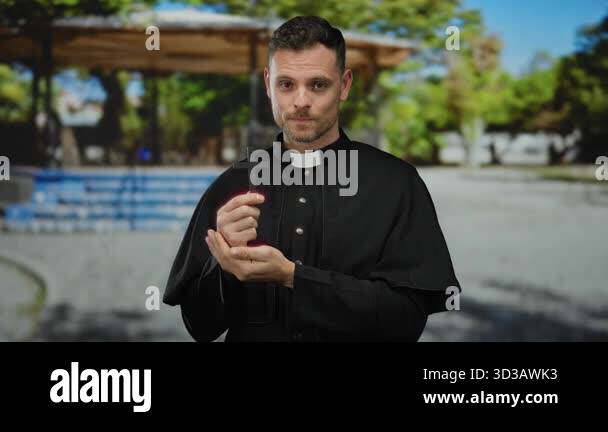 Catholic priest in black robe holding a cross in an outdoor park ...