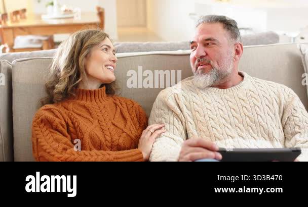 Resting hand on his arm, couple conversing on couch with tablet ...
