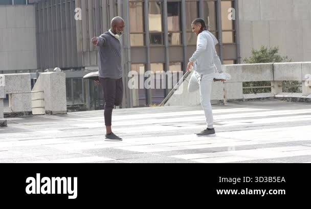 African American trainer and trainee stretching legs on plaza then ...
