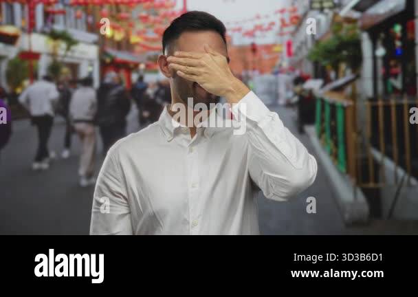 Young man in white shirt covers face on bustling city street with ...