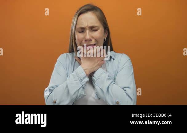 Woman choking on orange background showing pain and distress with hands ...