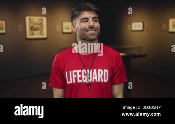 Young hispanic man wearing red lifeguard shirt and whistle smiles while ...