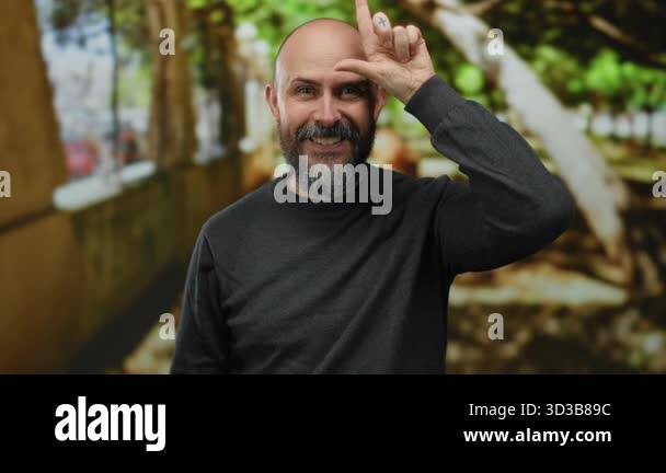 Bald man with beard playfully making loser gesture on urban street with ...