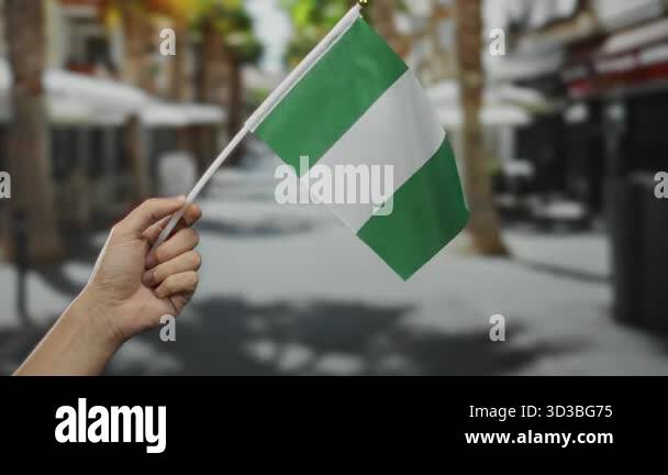 Hand holding a nigerian flag outdoors on a city street, capturing a ...