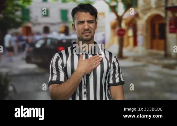 Young hispanic man in referee uniform stands on a bustling city street ...