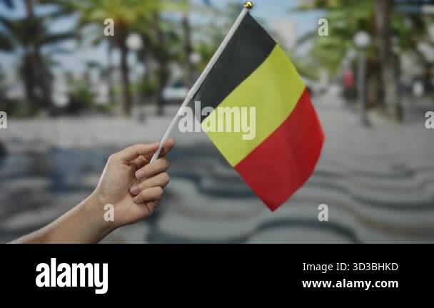 Hand holding belgian flag in an outdoor city street setting with ...