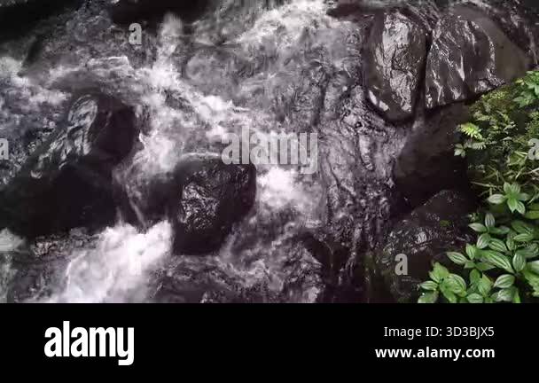 Rapid stream water forcefully splashing and swirling over dark wet ...