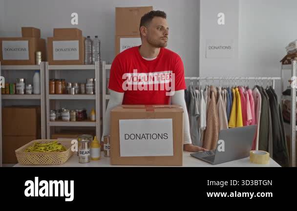 Young man volunteering in a charity room with donation boxes wearing a ...