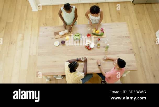 Diverse friends gathering around wooden table in bright kitchen ...