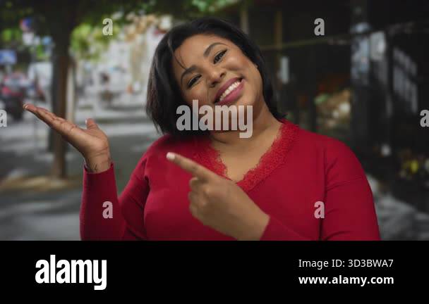 Woman smiling in vibrant red sweater gestures invitingly on a bustling ...