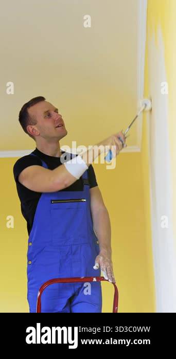 Man in work overalls paints the wall. Workman in the uniforms painting ...