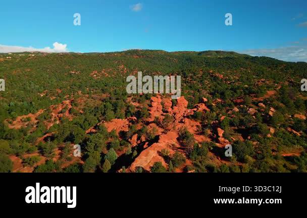 Approaching red clay rounded rocks lit with sun. Vegetation covers the ...