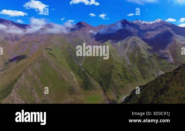 Drone footage captures a mountain valley with green slopes, clouds over ...