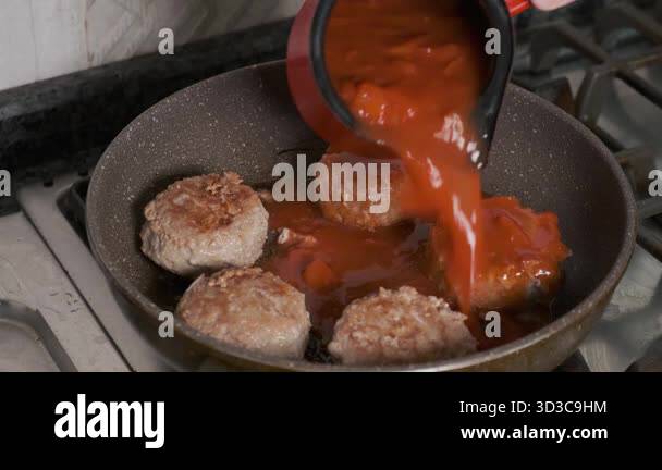 Man adding tomato paste and chopped tomatoes to meatballs frying in a ...