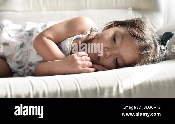 Sleepy child resting on a couch, eyes half open in soft daylight, calm ...