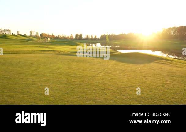 Golden hour over a lush golf course landscape with a flag marking the ...