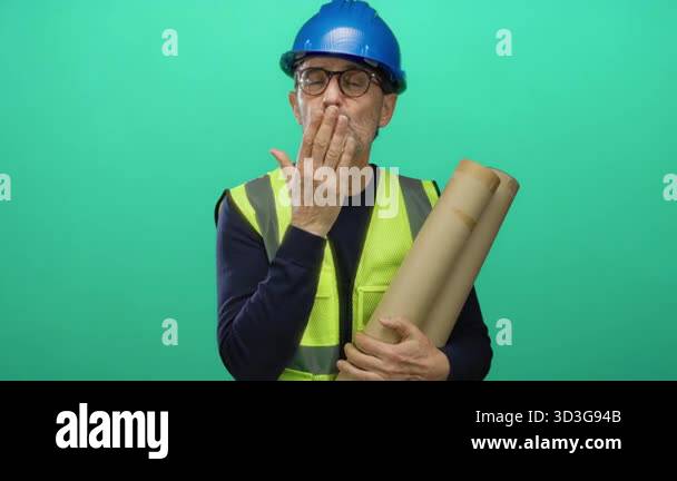 Man wearing blue helmet and safety vest holds rolled blueprints against ...