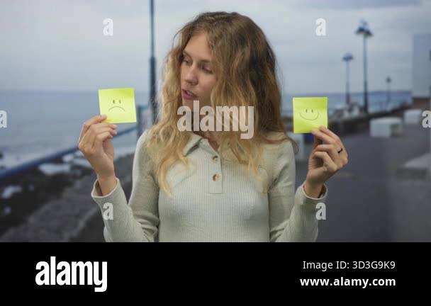 Woman holds note comparing emotions on a pier while the blonde young ...
