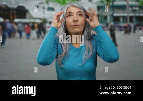 Woman with grey hair gestures expressively outdoors on a busy city ...