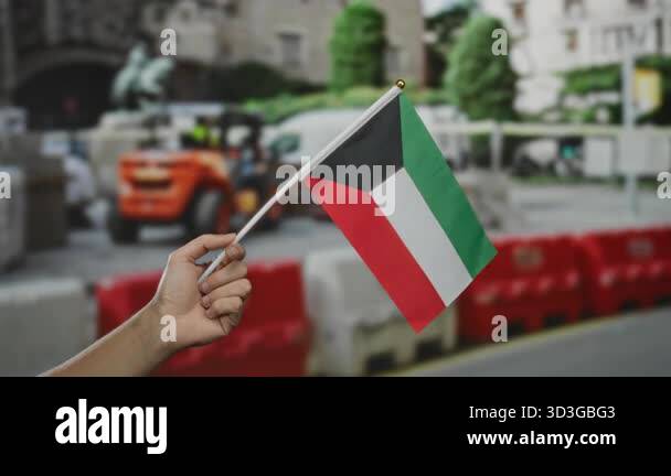 Man holding kuwaiti flag at construction site with blurred street ...