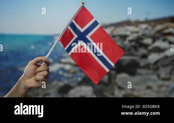 Hand holding norwegian flag by the seaside beach in norway, showcasing ...