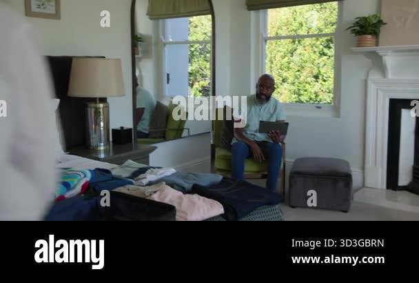 Diverse senior couple entering bedroom with two devices, perching on ...