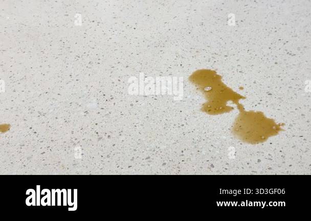 A hand wipes coffee spill on a light countertop using a paper towel ...