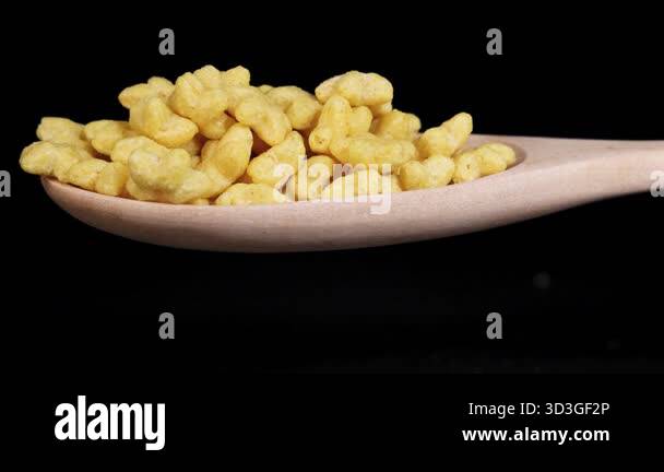 Star-shaped cereal pieces fall from a wooden spoon against a black ...
